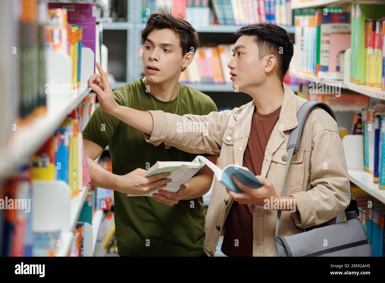 Teenage boy helping classmate to find book in library Stock Photo - Alamy