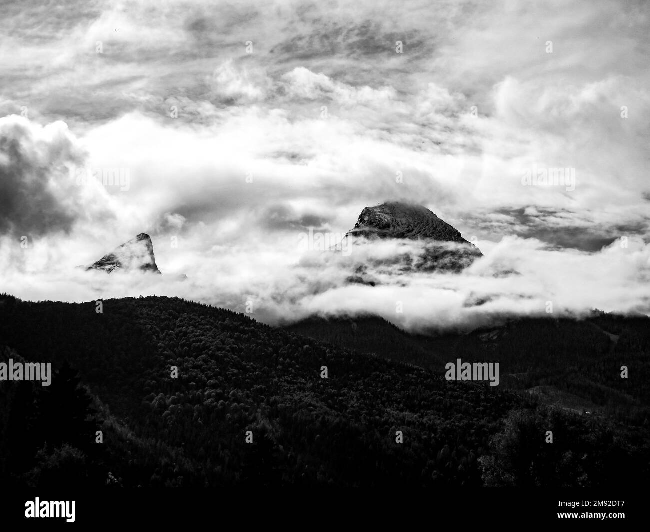A grayscale aerial view of a mountain summit covered with clouds on a ...