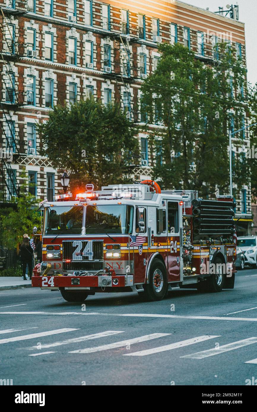 Bright red fire engine with glowing headlights on asphalt road in city ...