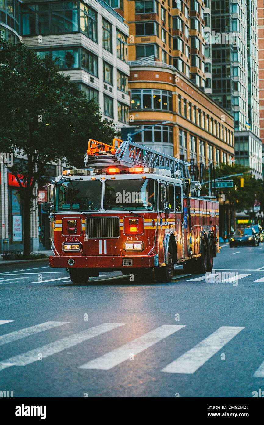 Bright red fire engine with glowing headlights on asphalt road in city ...