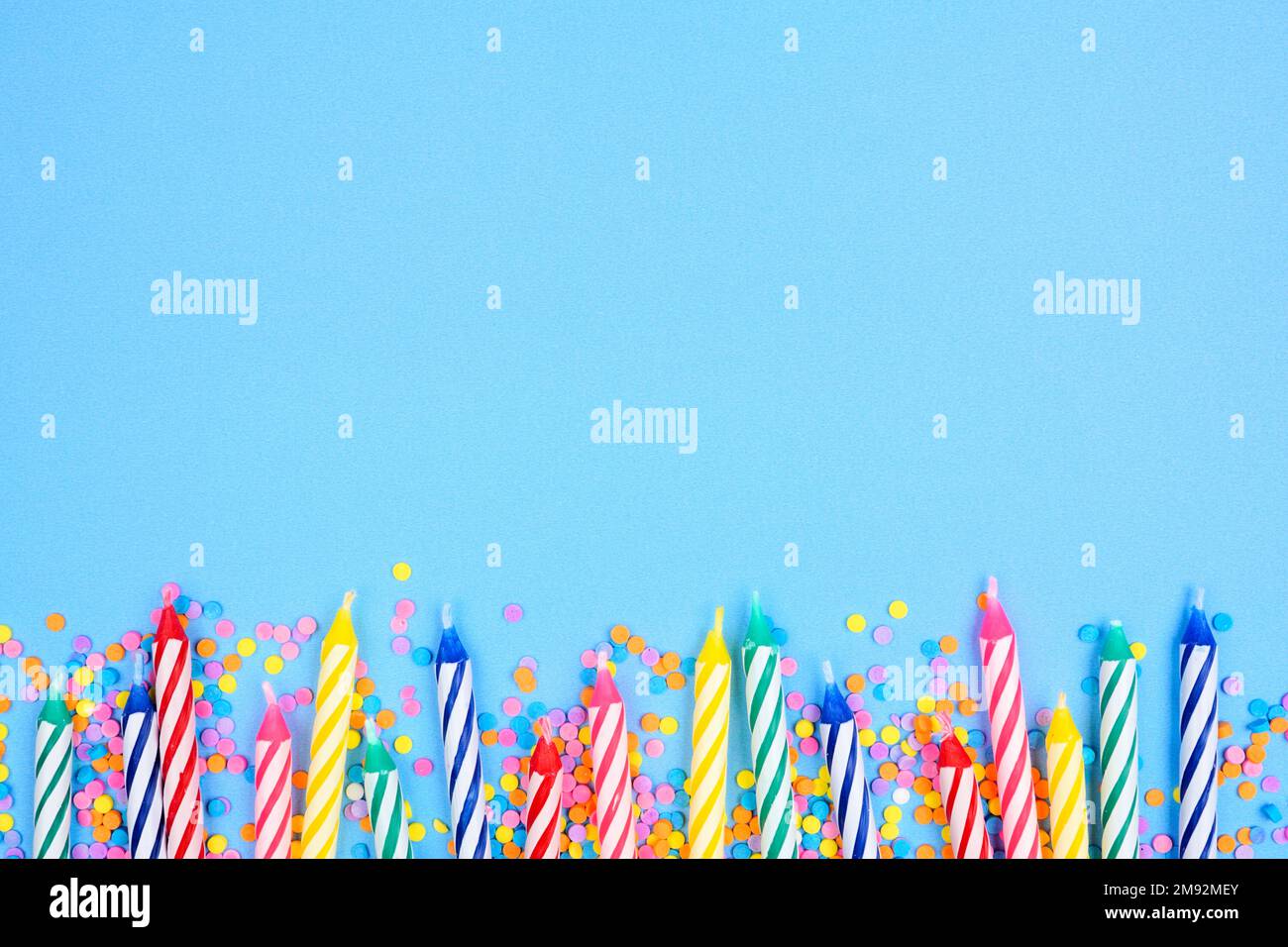 Birthday cake candles with candy sprinkles. Above view bottom border on a blue background. Copy ...