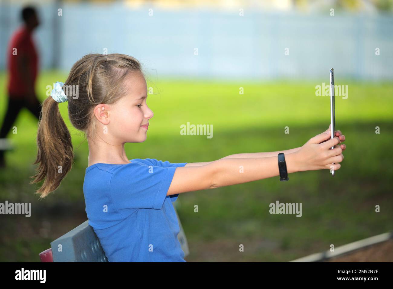 Happy child girl looking at screen of digital tablet resting on bench ...