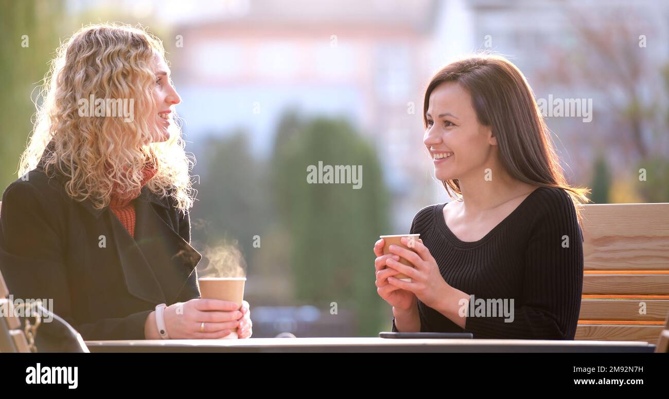 Happy young women friends drinking coffee at city street restaurant ...