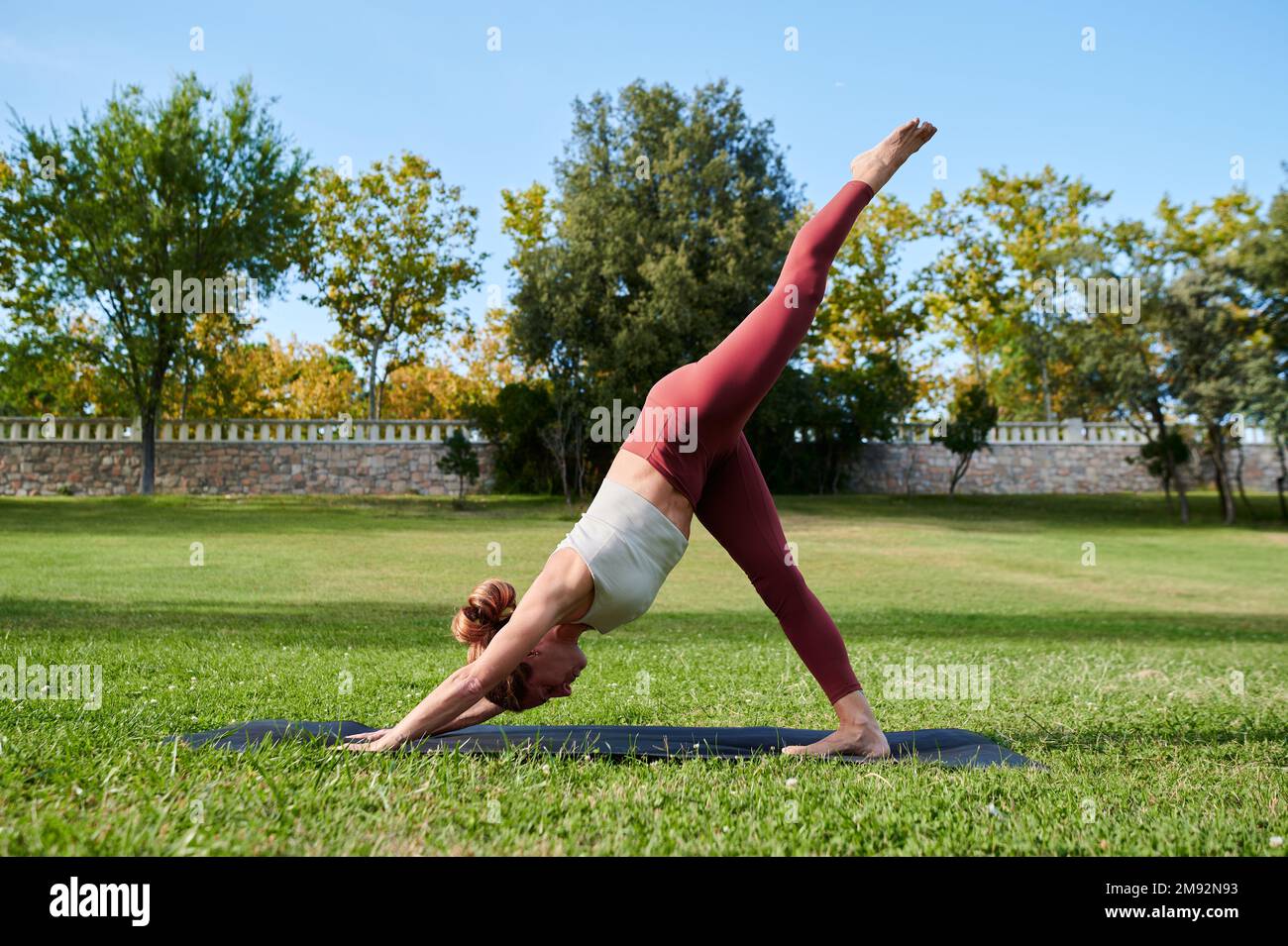 Full body side view of young flexible woman doing yoga in Downward ...