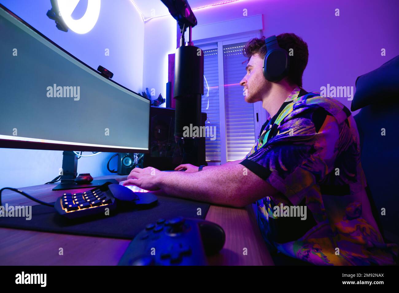 Low angle side view of young male gamer in colorful shirt and wireless ...