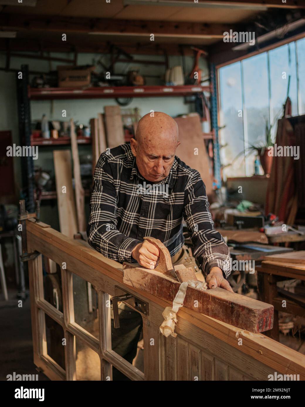 Elderly male woodworker in checkered shirt cutting wooden plank with ...