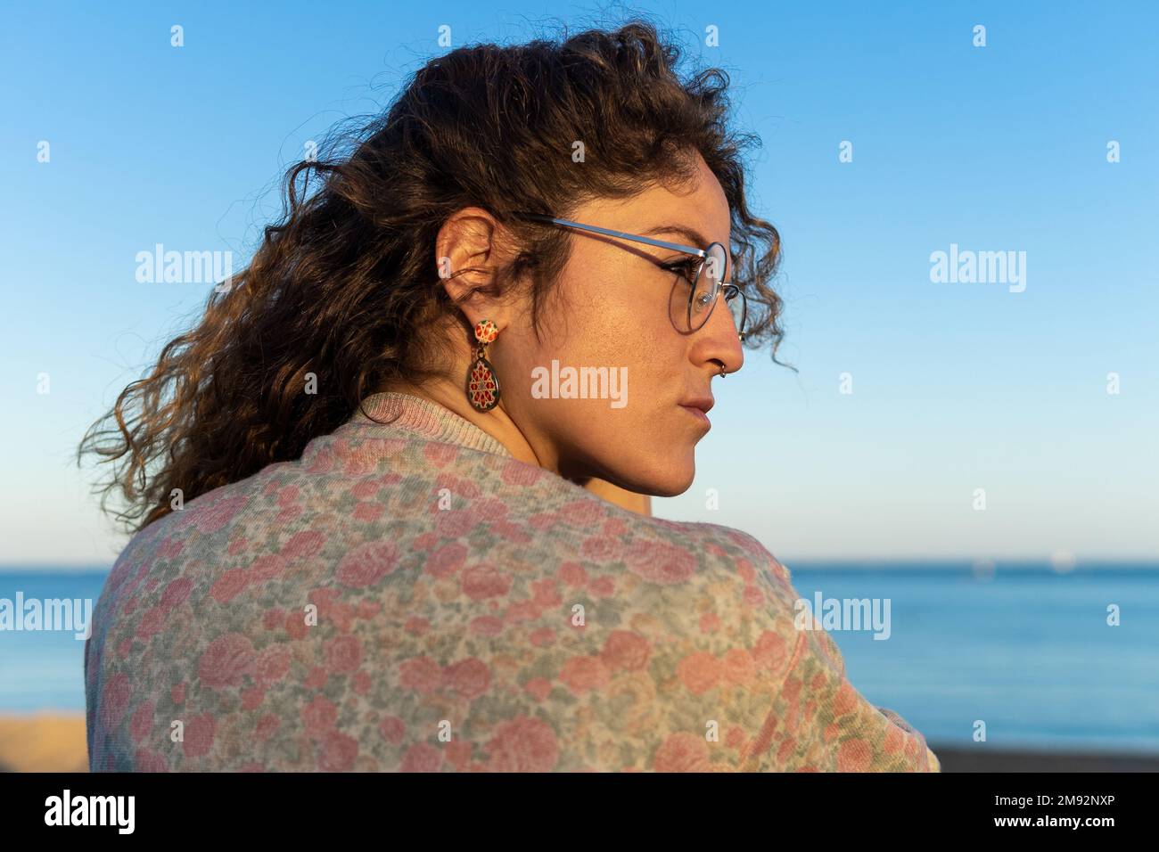 Side view of young dreamy female with curly hair in glasses and casual ...