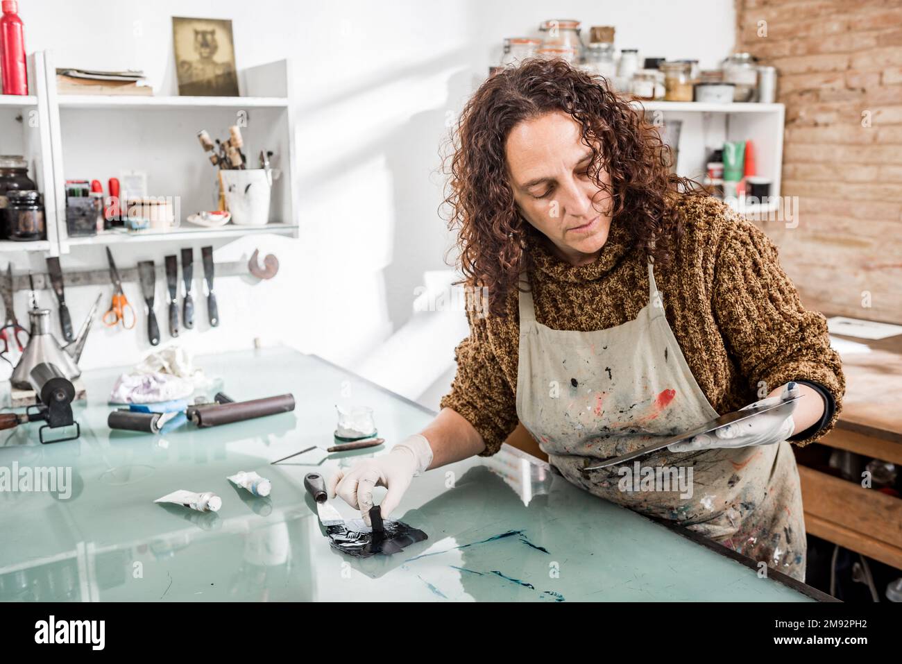 Middle aged craftswoman in dirty apron inspecting metal plate for ...
