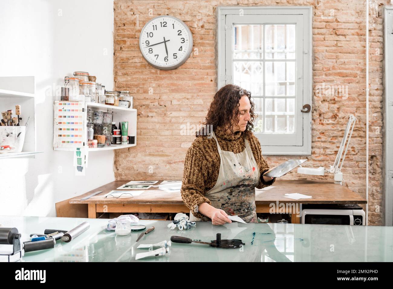 Middle aged craftswoman in sweater and apron examining photoengraving ...