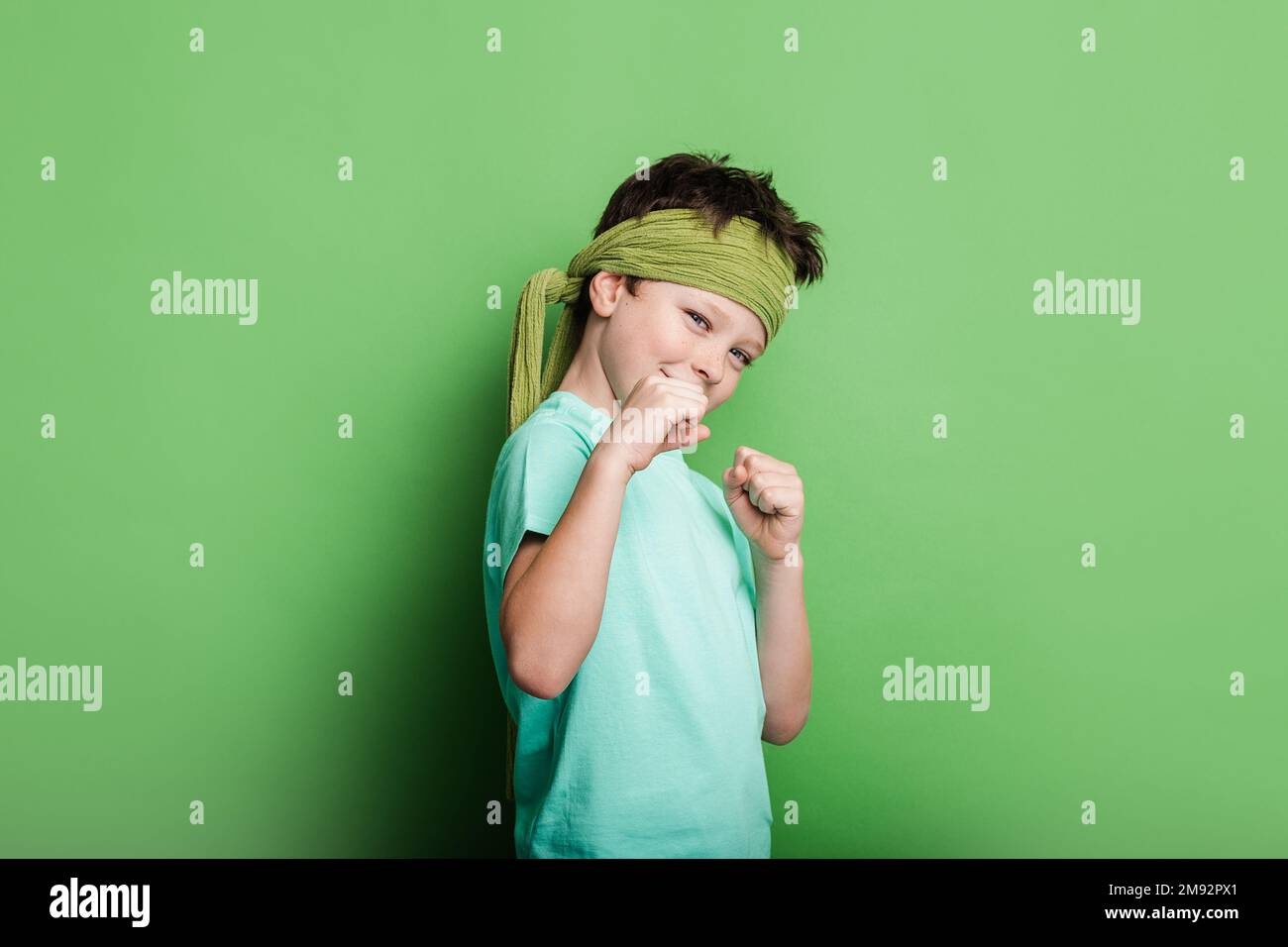 Cute boy in t shirt with headband standing in boxing pose ready defend ...