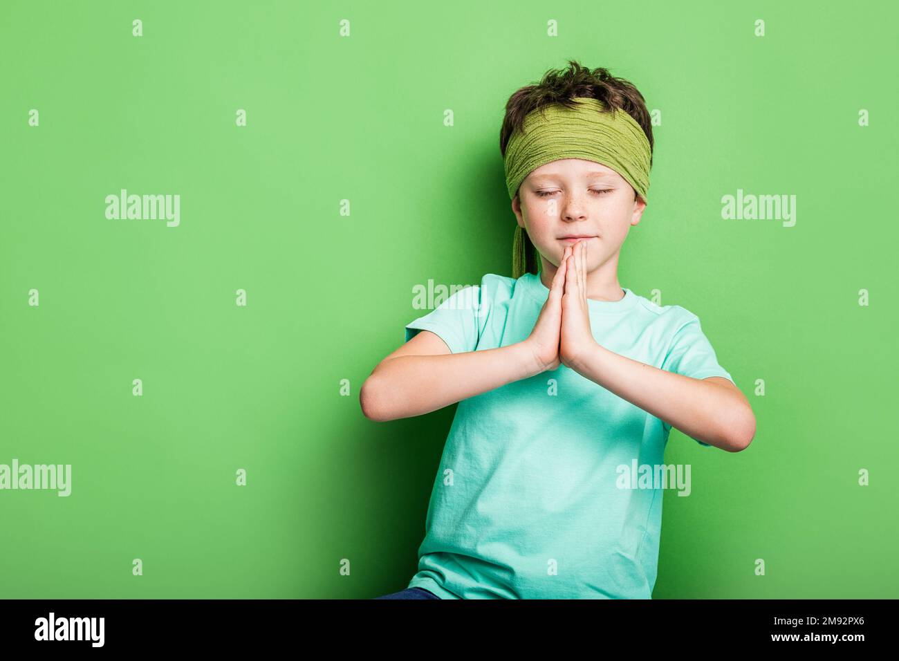 Calm boy with headband in casual clothes standing against green ...