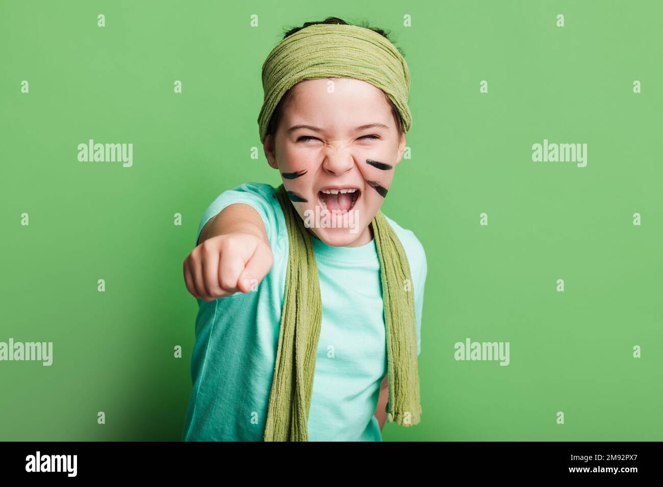 Cheerful child with headband and stripes on cheeks yelling with fist up ...