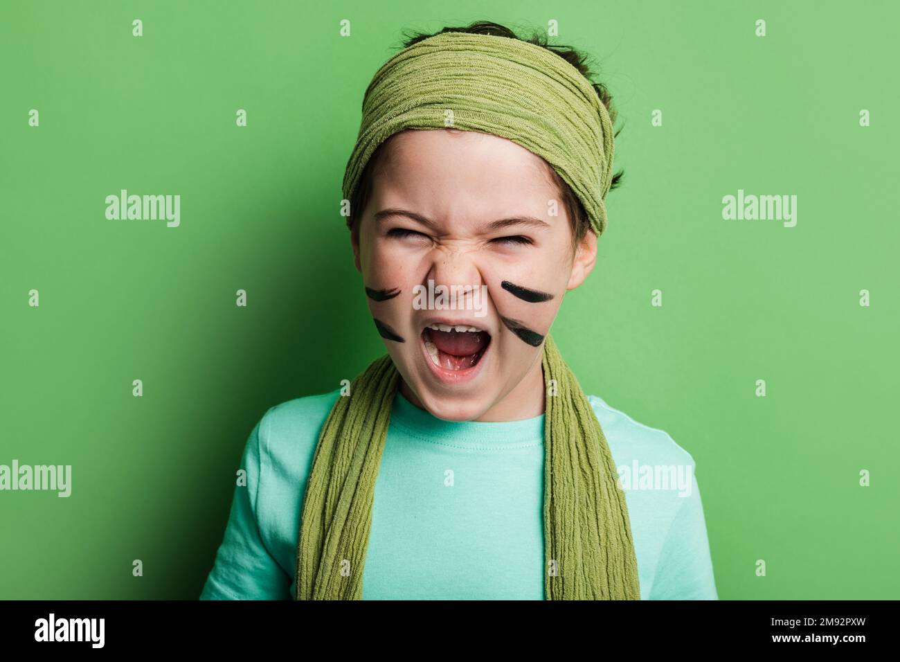 Playful little kid in casual clothes with headband and painted face ...