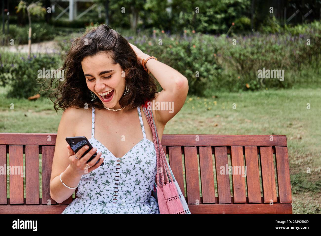 Cheerful young female in casual summer dress laughing and messaging on ...