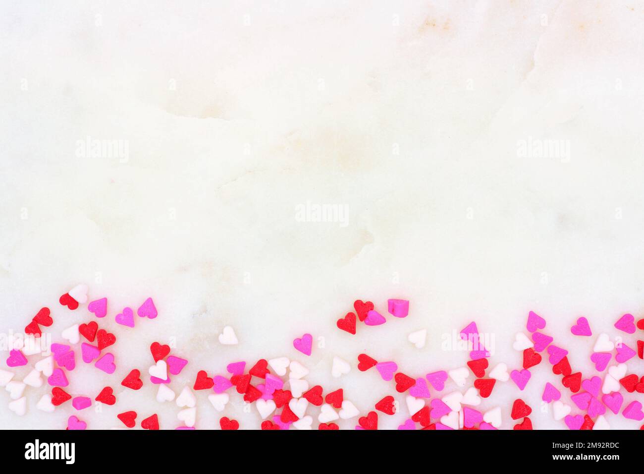 Valentines Day candy heart sprinkles bottom border over a white marble ...