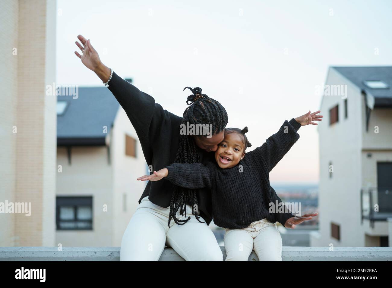 Black woman with Afro braids in casual wear sitting with cheerful girl ...