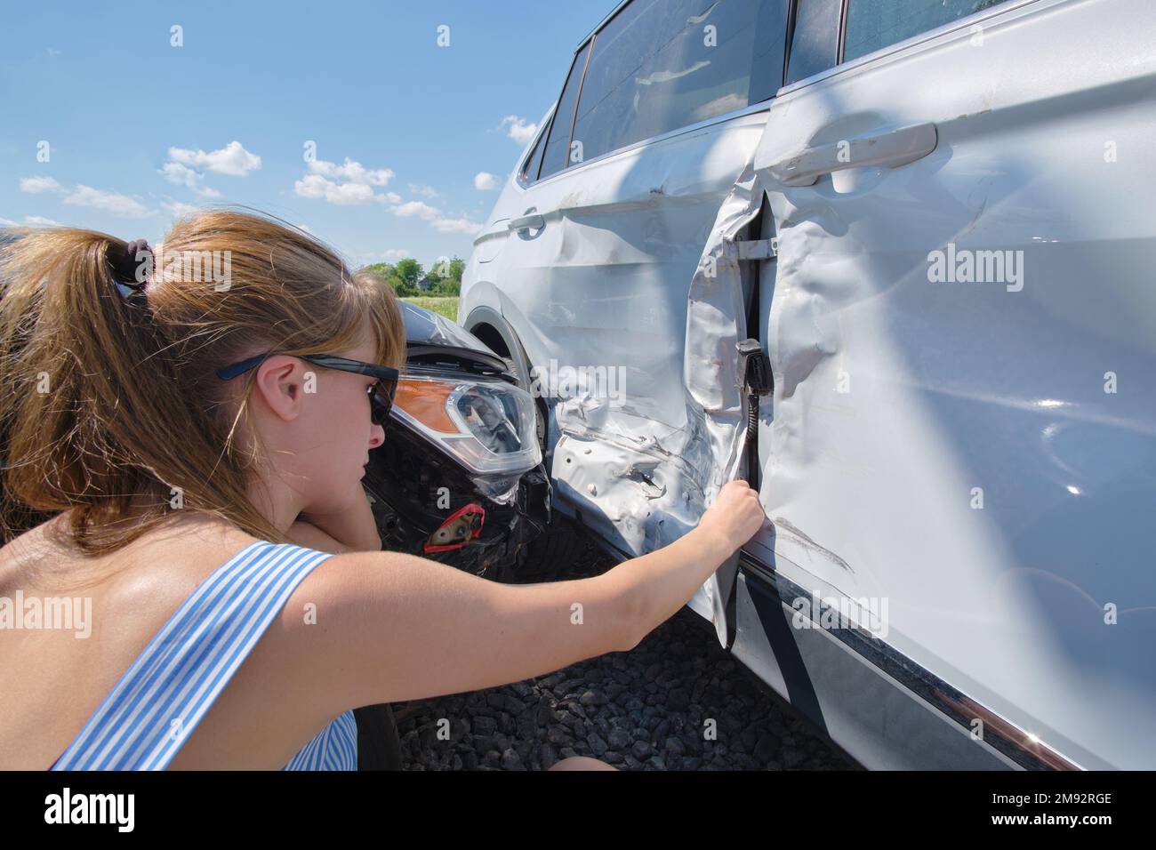 Sad young woman driver sitting near her smashed car looking shocked on ...