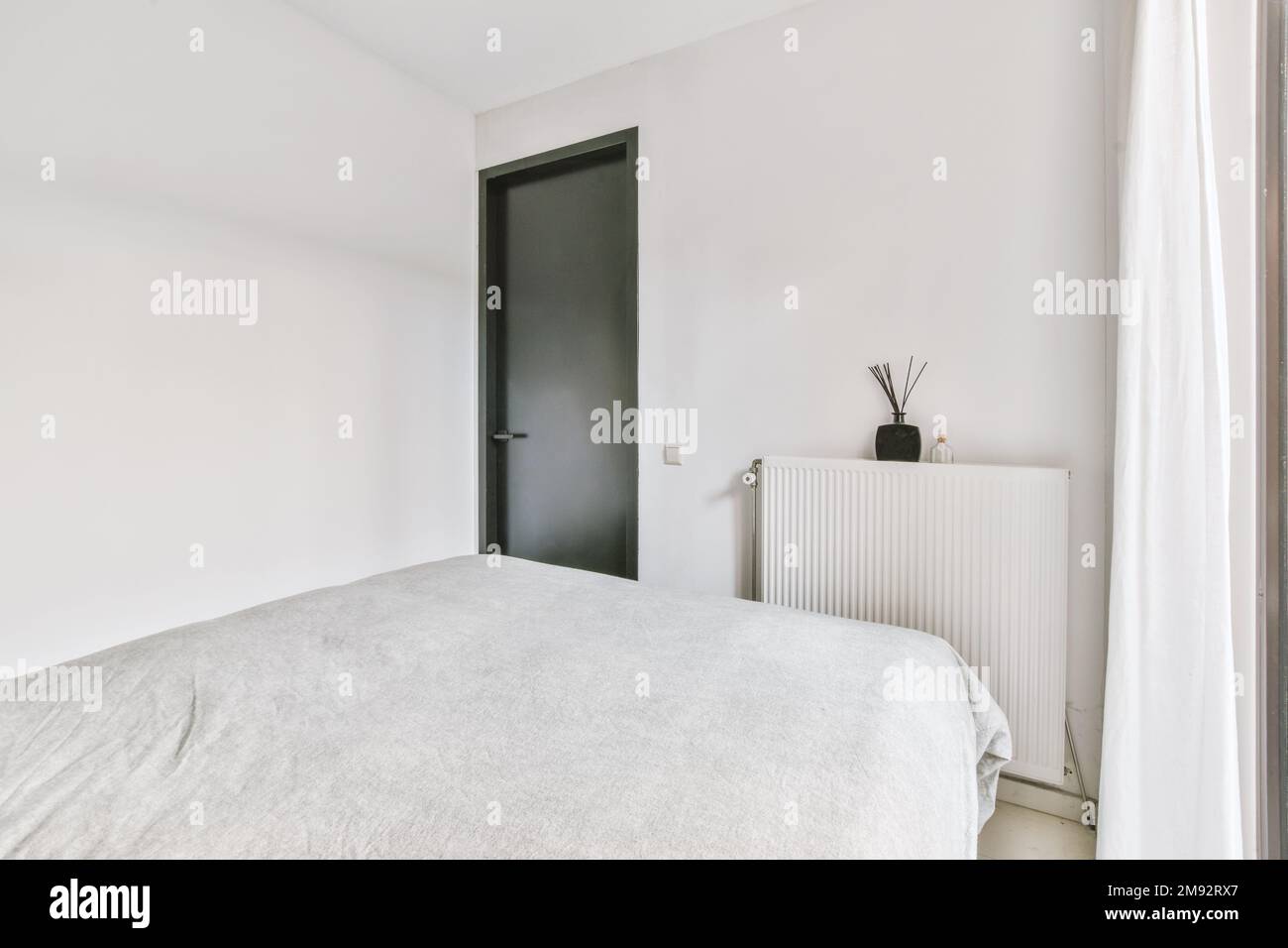 Comfortable bed covered with gray blanket near white radiator and black ...