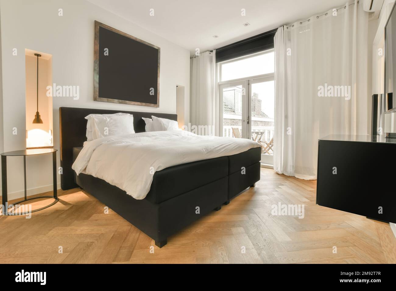 Comfortable bed next to a bright window and wooden floor Stock Photo ...