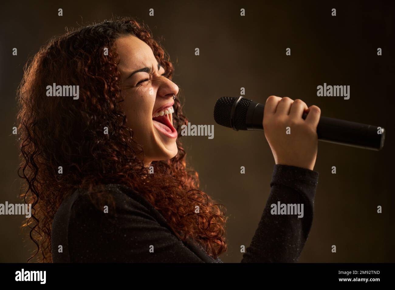 Side view of young female singer in black shirt with curly hair singing ...