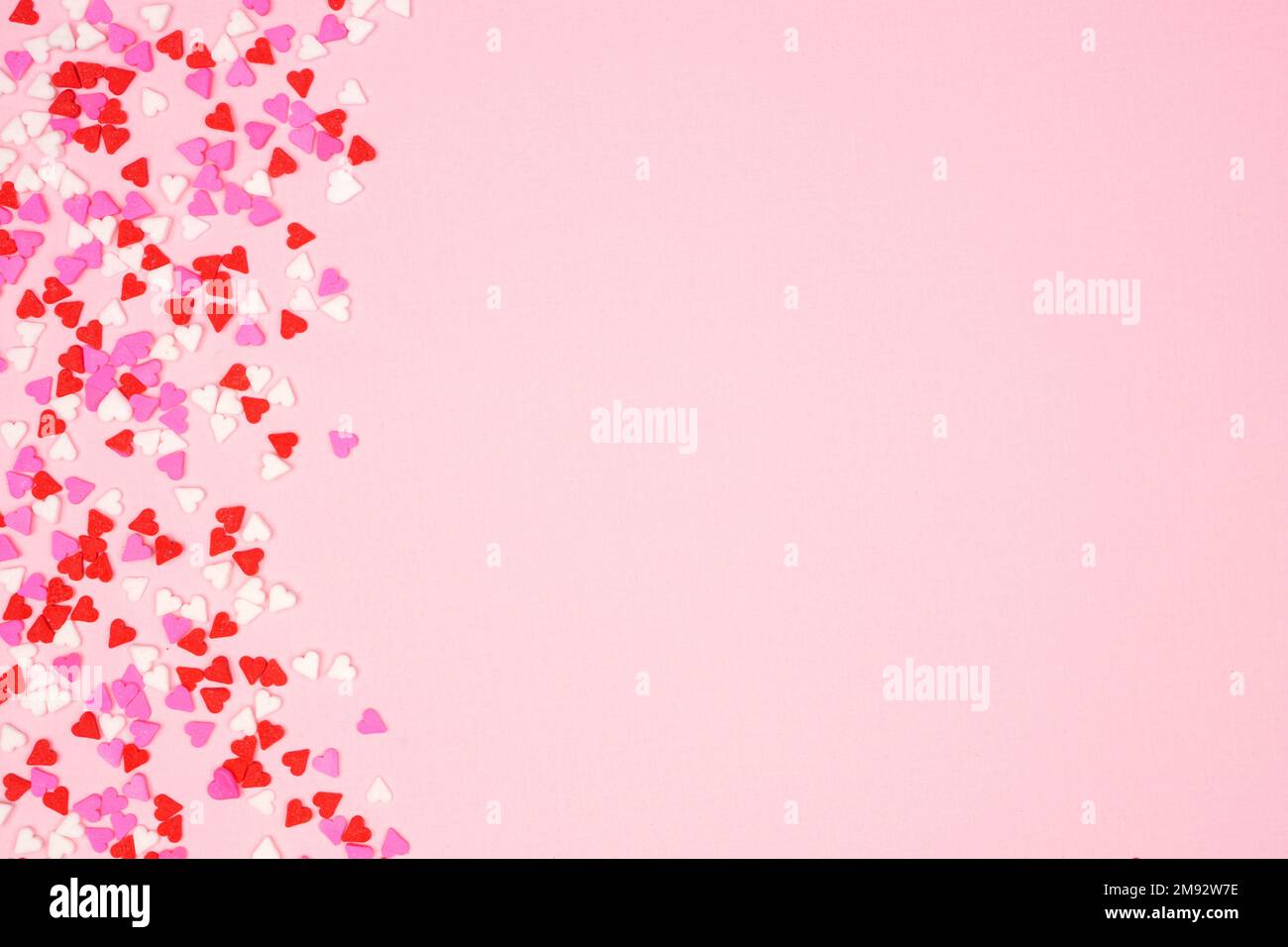 Valentines Day side border with candy heart sprinkles over a pink ...