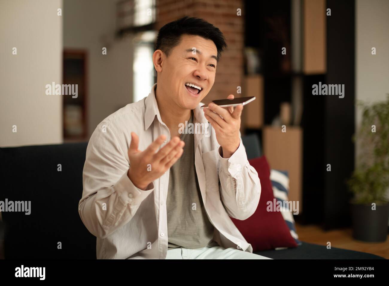 Portrait of happy asian man holding cellphone near mouth and recording ...