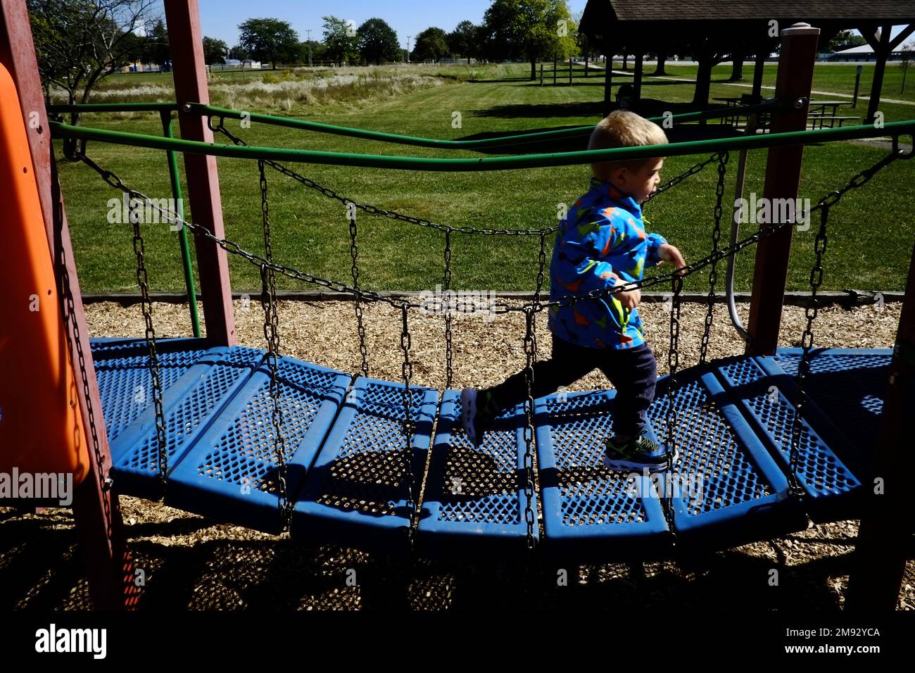 A three-year-old boy playing on playground equipment at a park in the ...