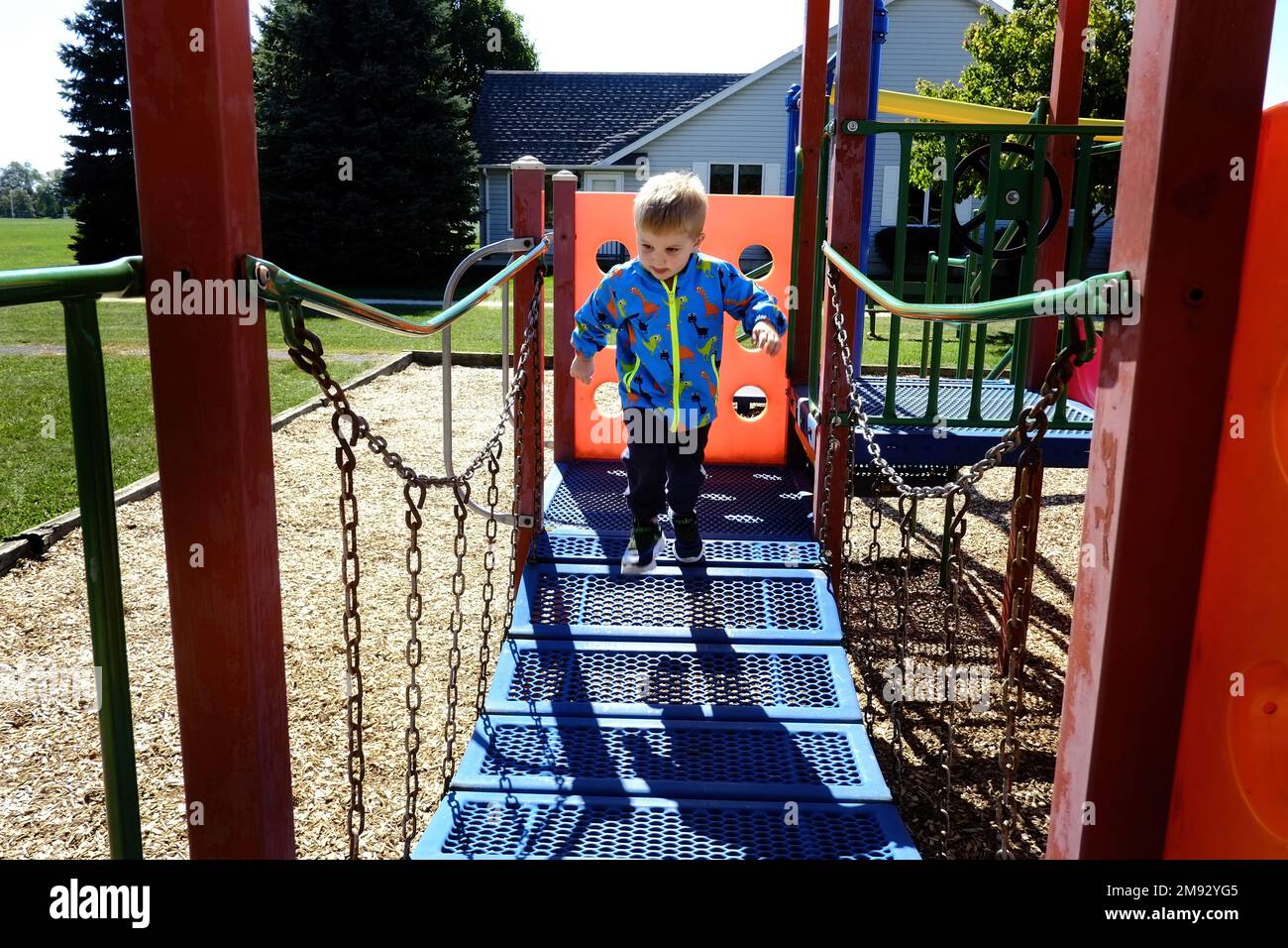 A three-year-old boy playing on playground equipment at a park in the ...