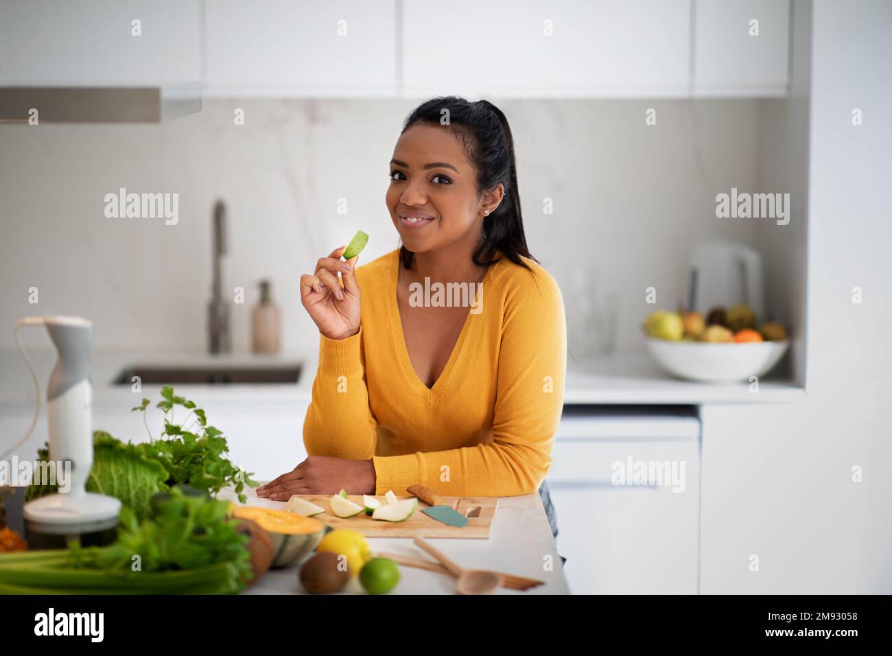 Smiling young african american female eating piece of fruit at table ...
