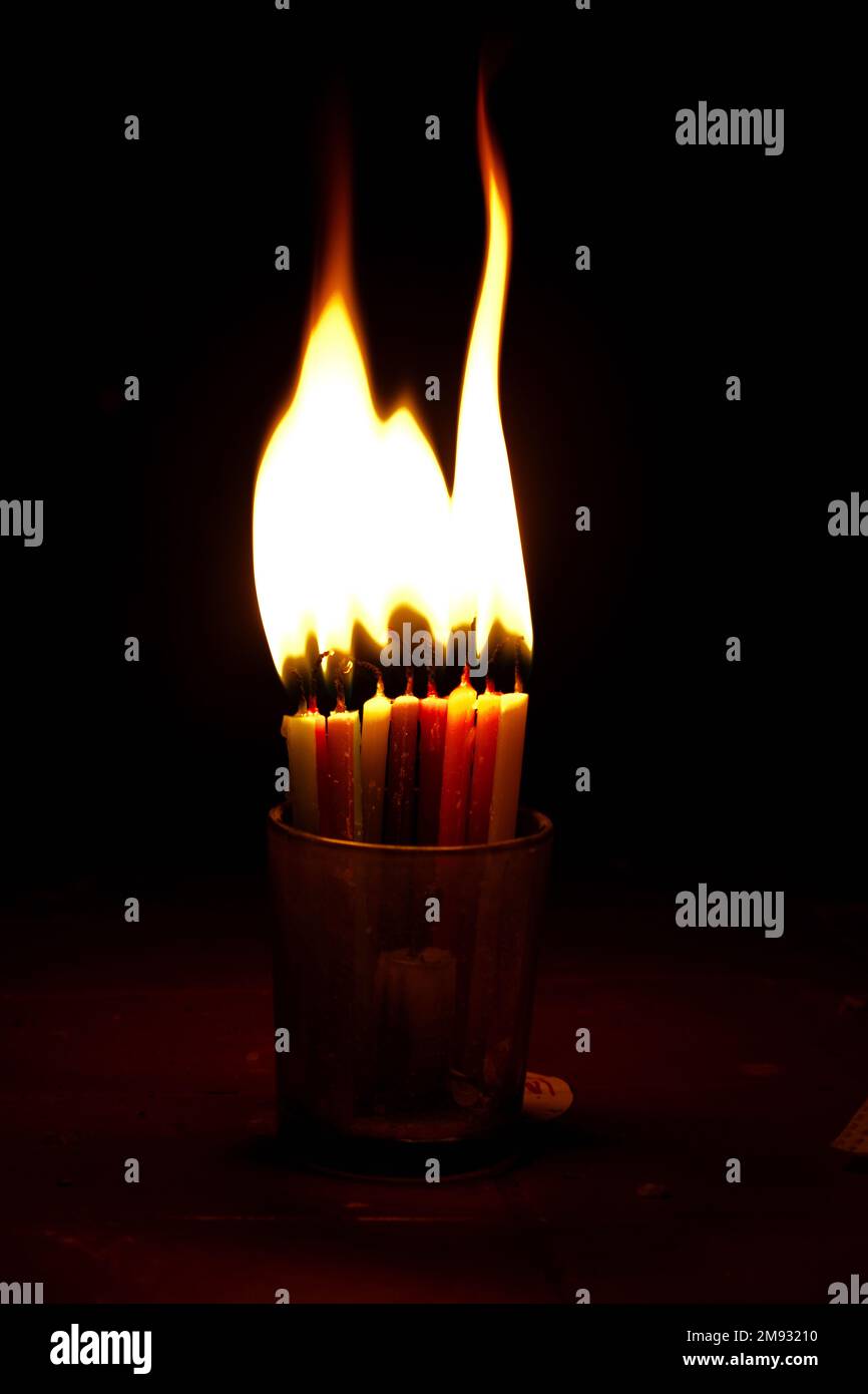 Burning multicolour small thin candle around dark place Stock Photo - Alamy