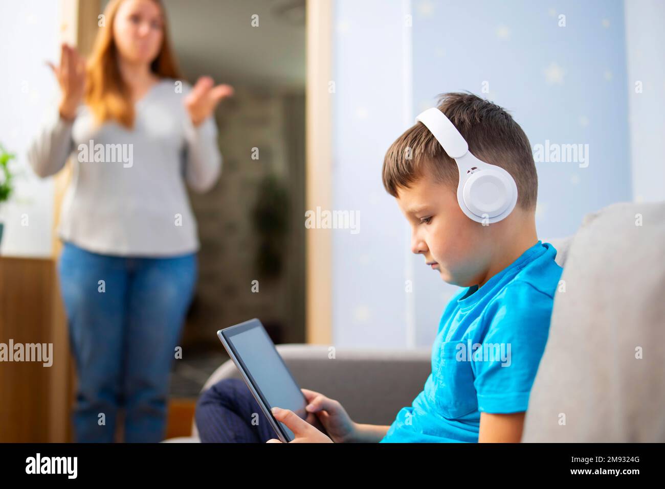Mother scolds her son. Boy uses tablet with headphones and ignores his ...