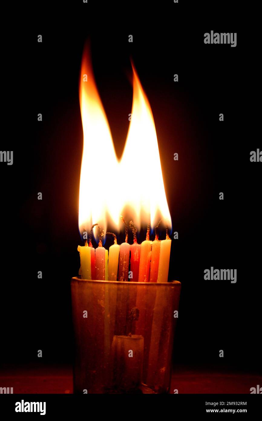 Burning multicolour small thin candle around dark place Stock Photo - Alamy