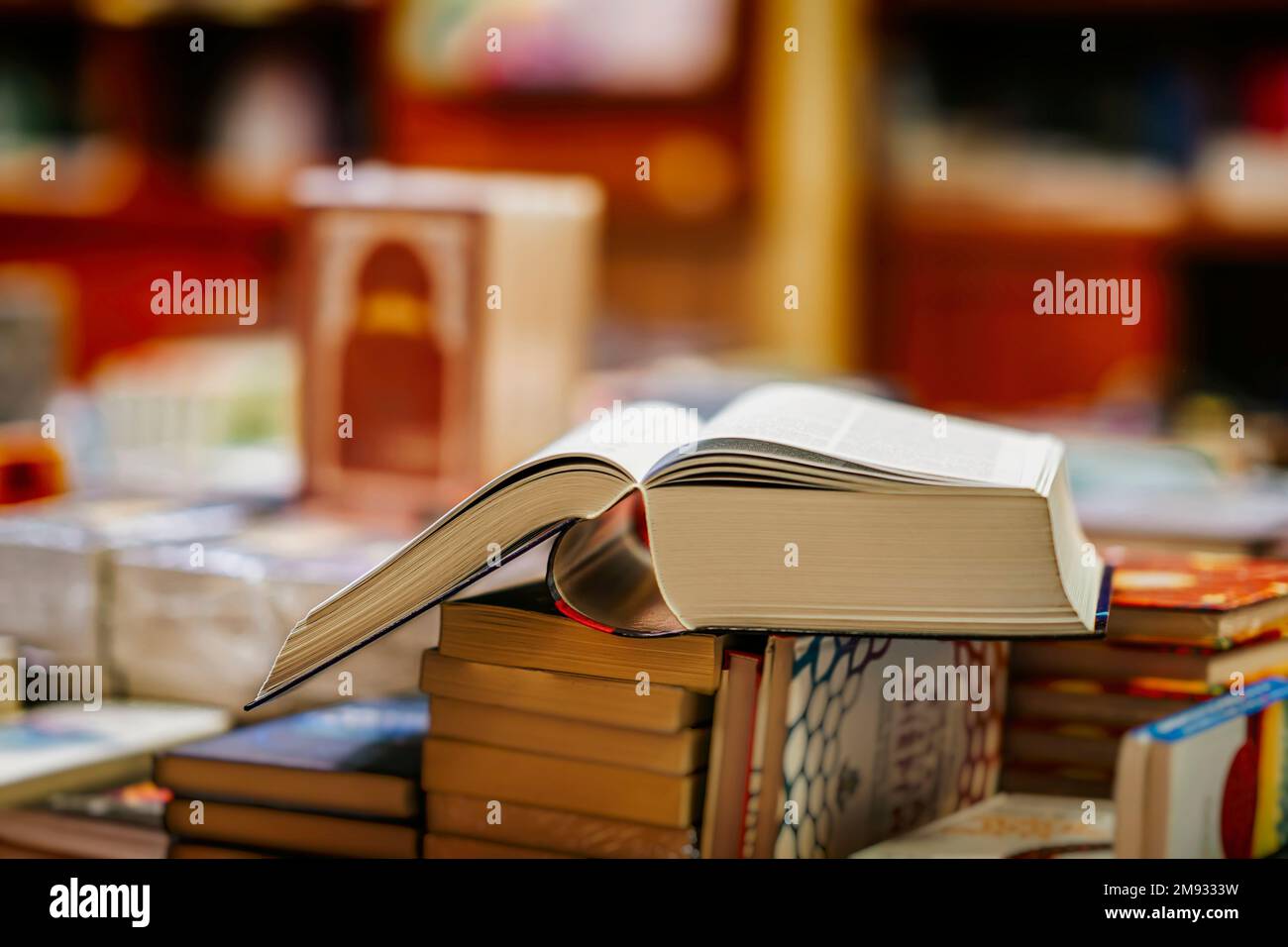 Open thick book on pile of books in book store or in library, selective focus, blurred ...