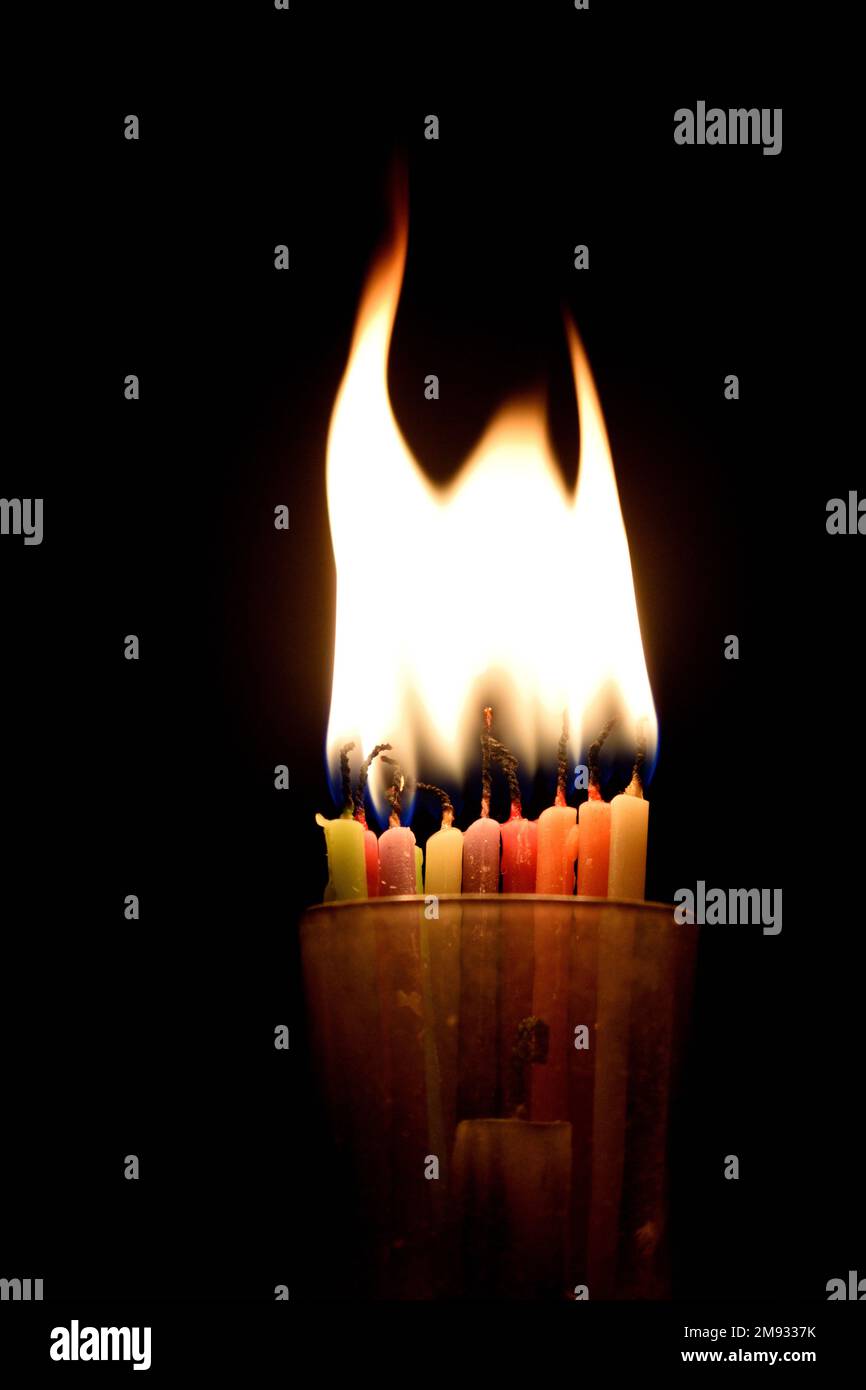 Burning multicolour small thin candle around dark place Stock Photo - Alamy