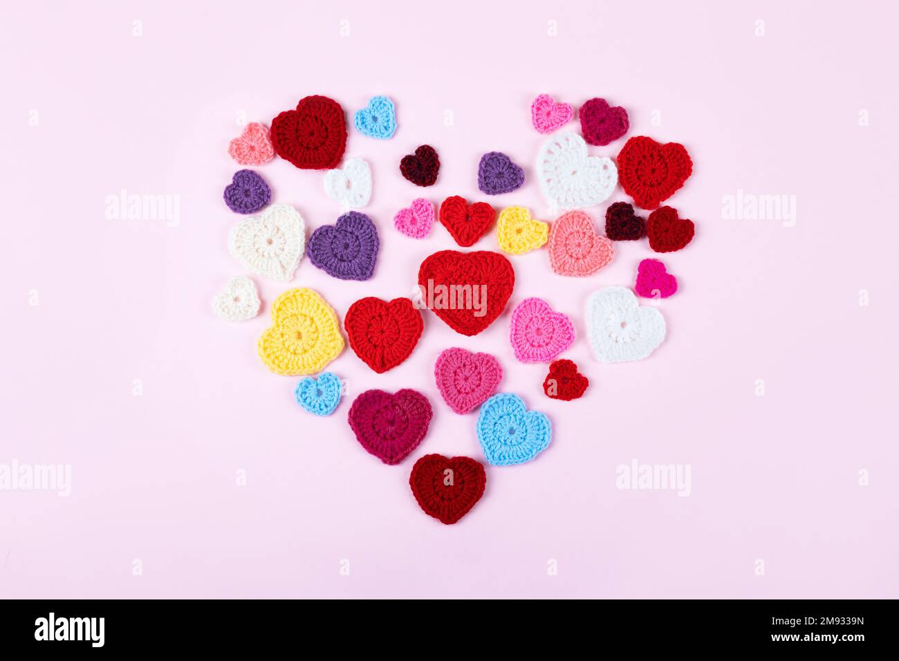 Multicolored crocheted hearts are laid out in the shape of a heart on a ...