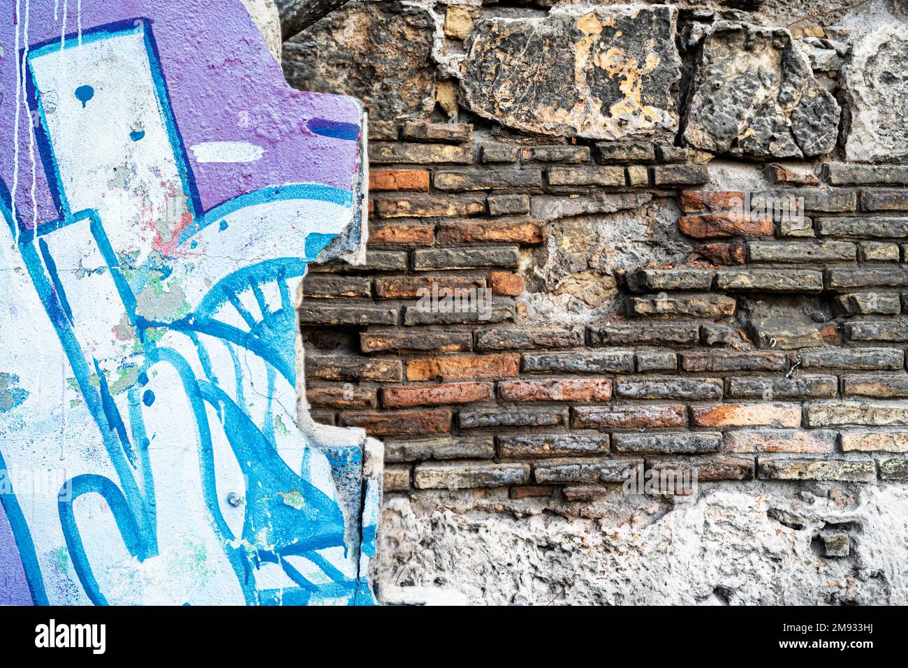 Wall in ruins colored with paint blocks hiding an ancient red brick ...