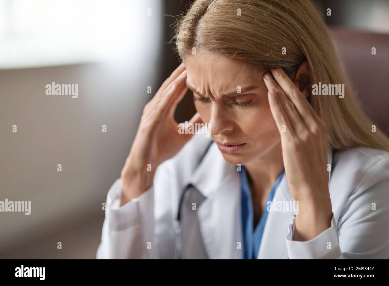 Portrait Of Stressed Female Doctor In Medical Coat Suffering Headache ...