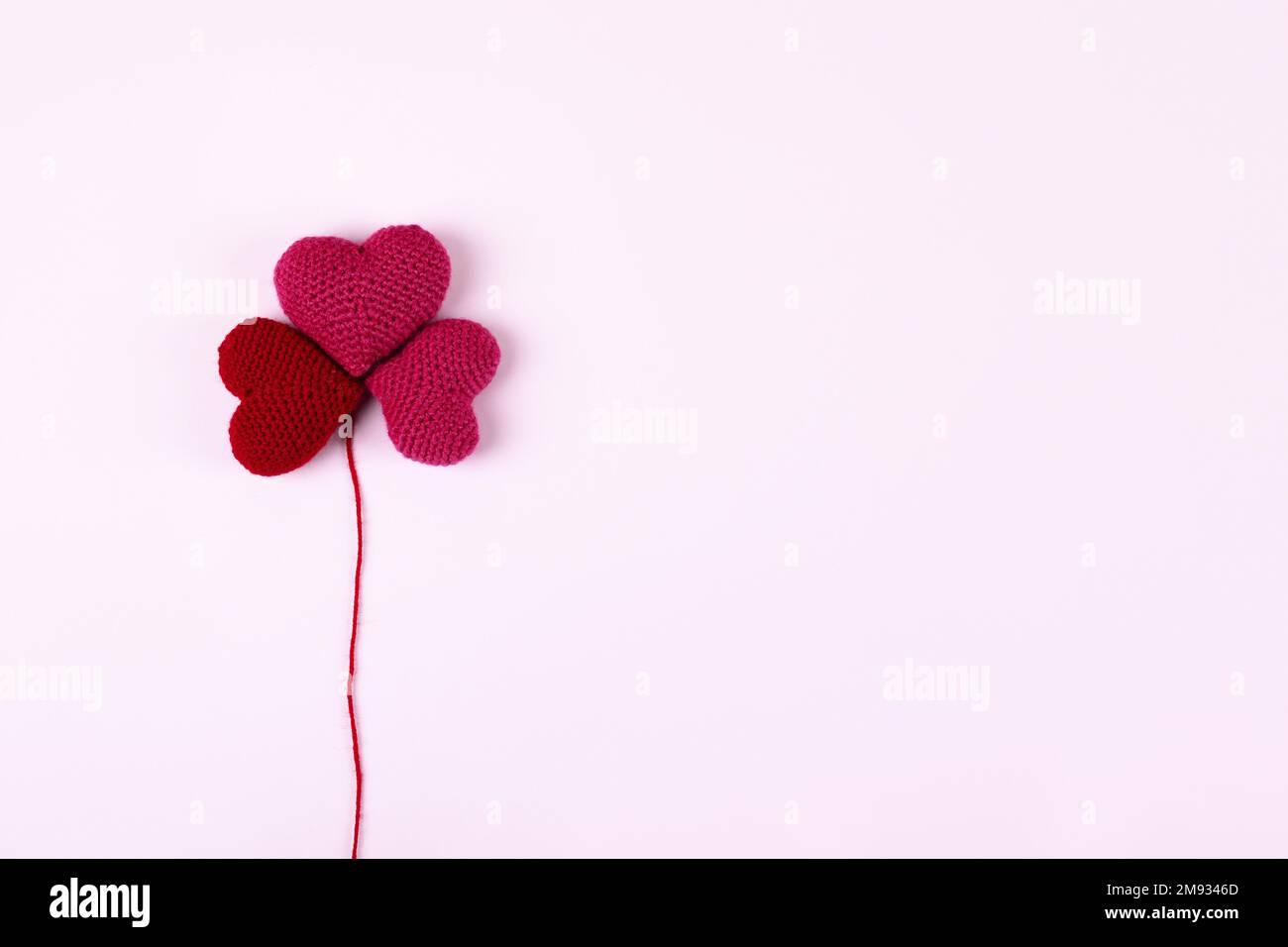 Red crocheted hearts are laid out in the shape of a flower clover on a ...