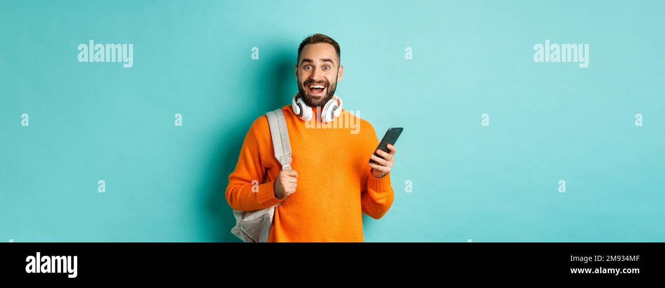 Caucasian man with headphones and backpack staring at camera amazed ...