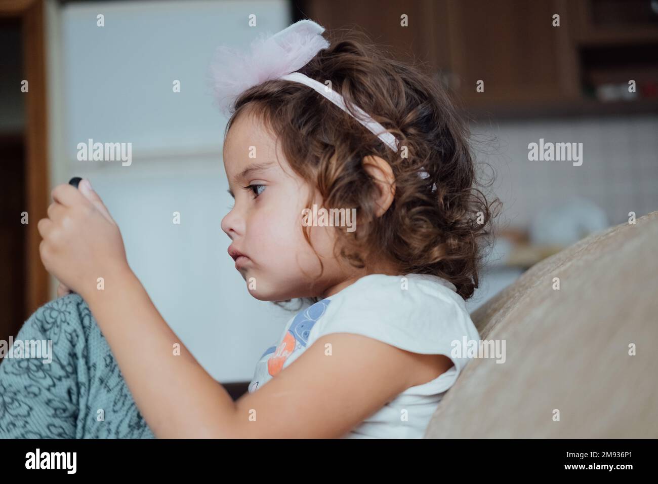 Cute little kid girl using mobile phone sitting on sofa alone Small ...