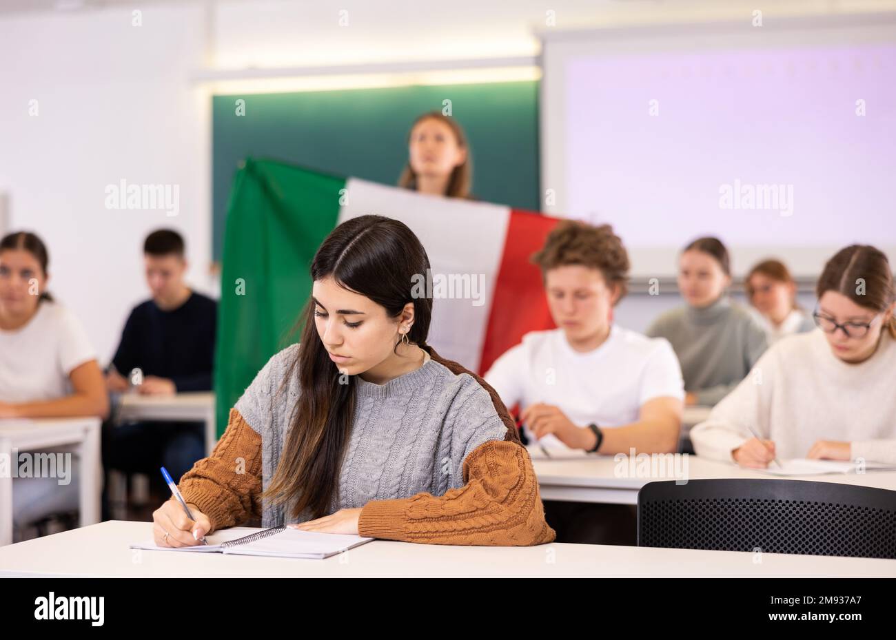 High school teacher tells students about Italy and holds a Italy flag ...