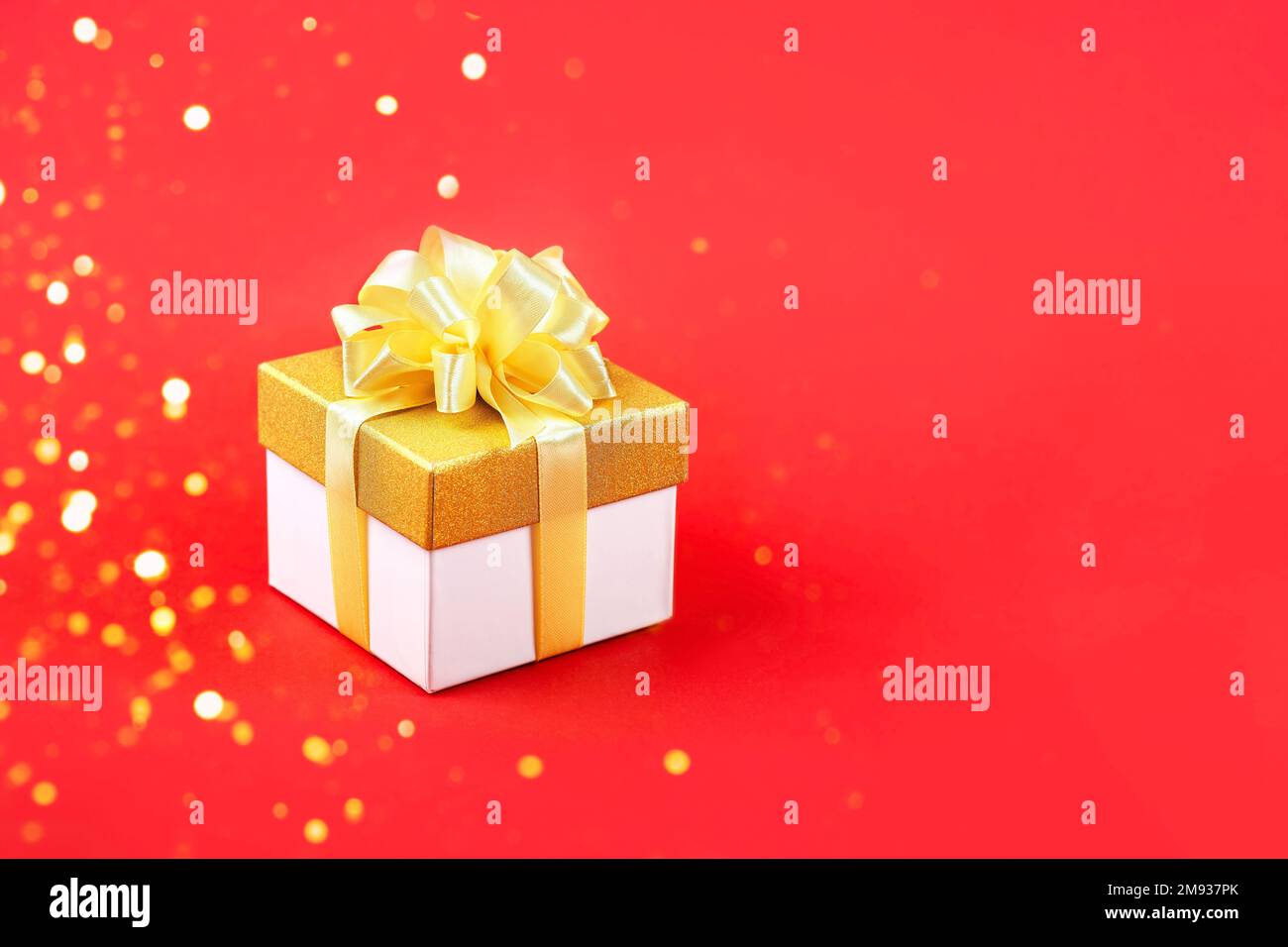 Golden gift box with a satin ribbon bow on red background for a holiday ...