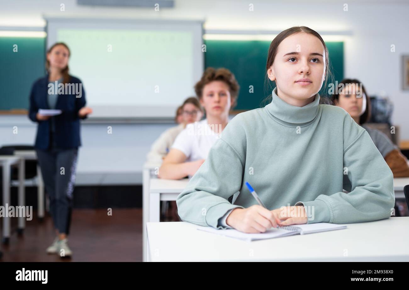 Girl and boy sitting at lesson in classroom, teacher standing Stock ...