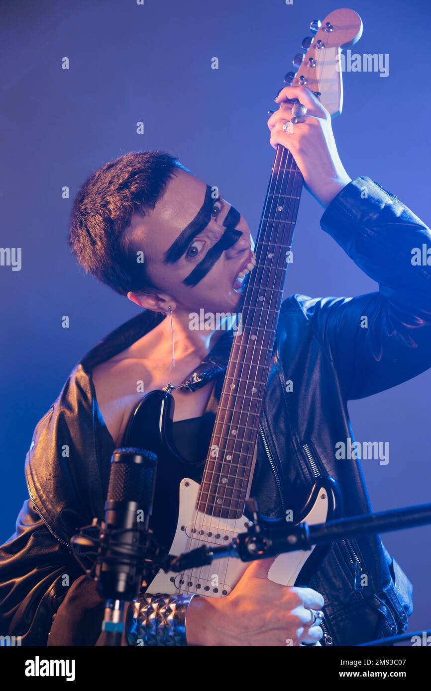 Crazy rocker biting on guitar instrument in studio, acting silly and ...