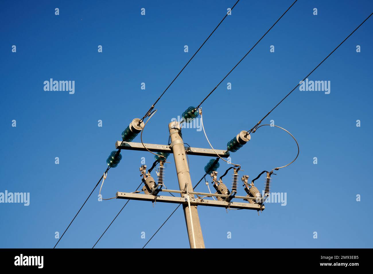 Looking up at concrete power pole and powerlines against clear blue sky ...