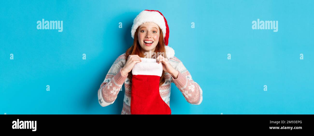 Beautiful redhead girl in santa hat open Christmas stocking and looking ...