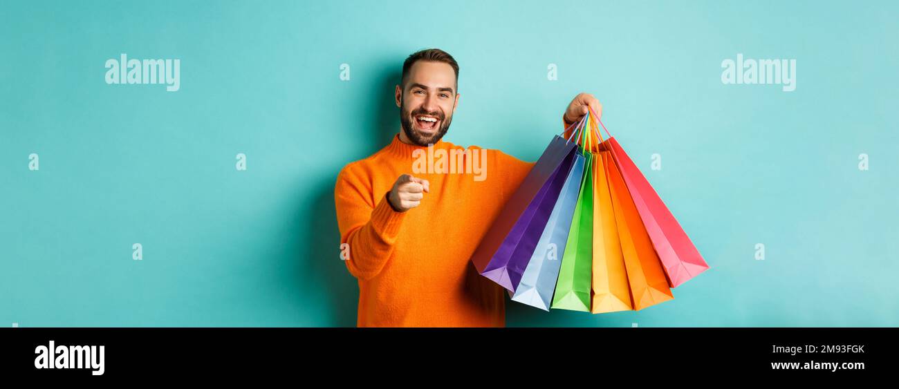 Happy adult man pointing finger at camera, holding shopping bags and ...