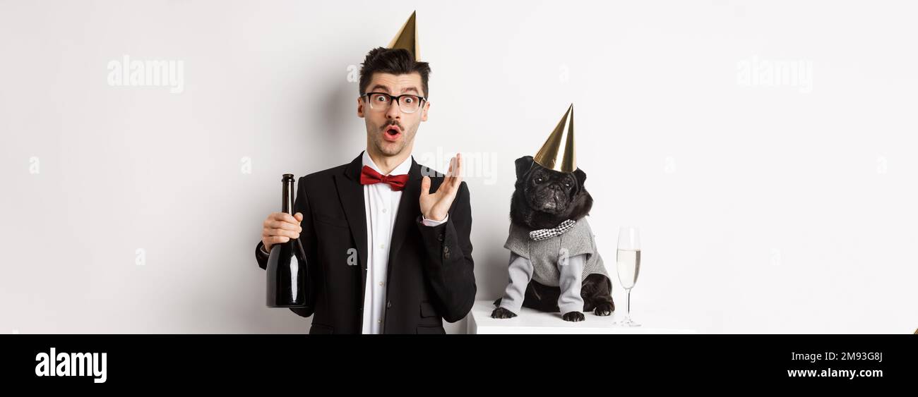 Happy young man celebrating holiday with cute dog, holding champagne ...