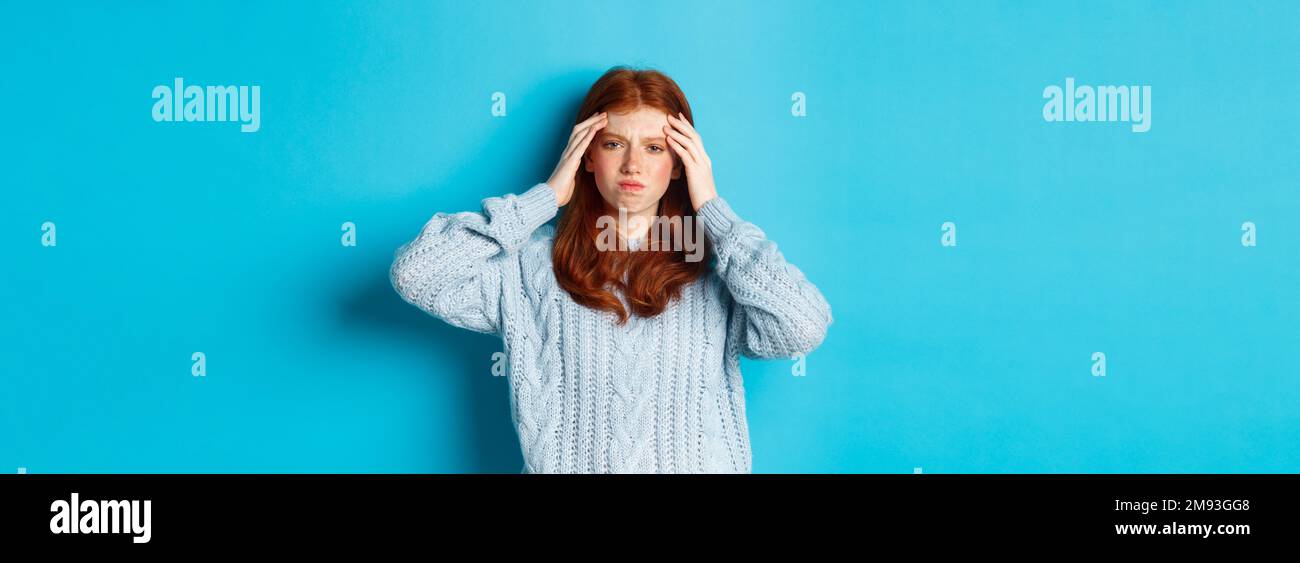 Distressed teenage redhead girl touching head, looking with troubled ...