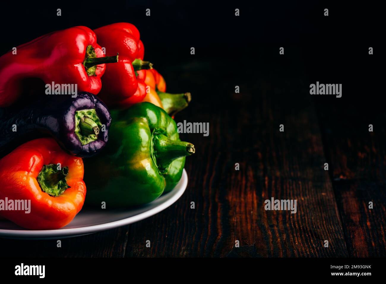 Multicolored fresh bell peppers on plate over wooden background Stock ...